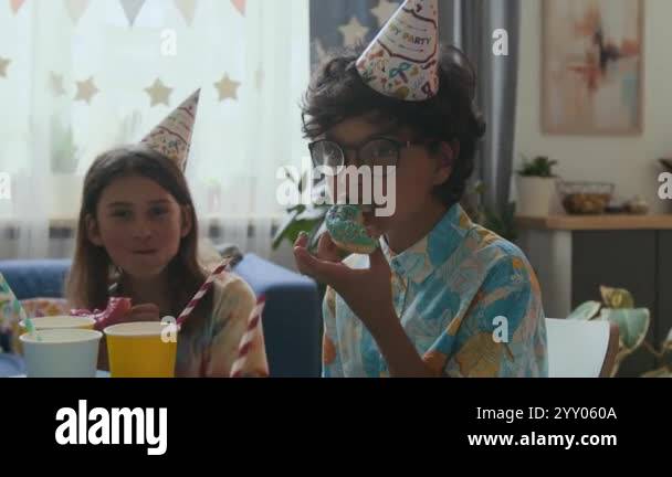 Two gen alpha boys wearing party hats eating donuts while celebrating ...