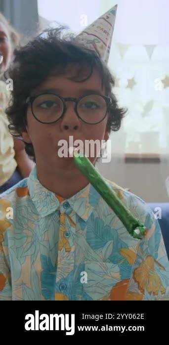 Vertical portrait of gen alpha boy with party hat blowing whistle and ...