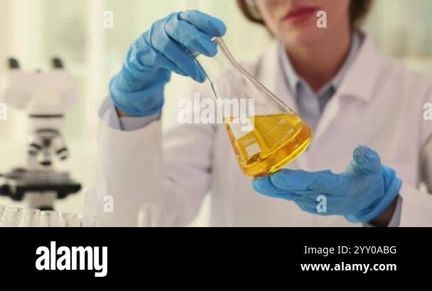 Woman scientist tilts flask containing yellow liquid. Female ...