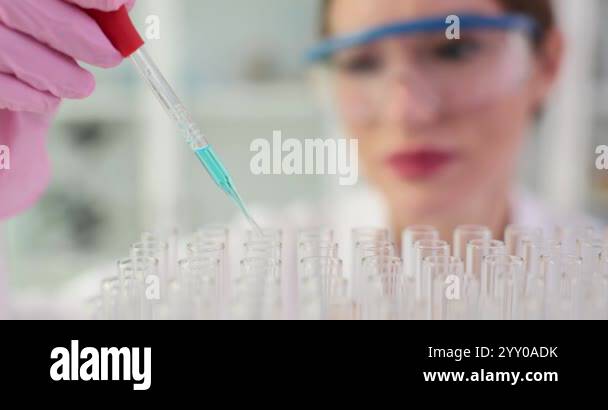 Lab technician drips blue liquid into test tubes using pipette. Woman ...