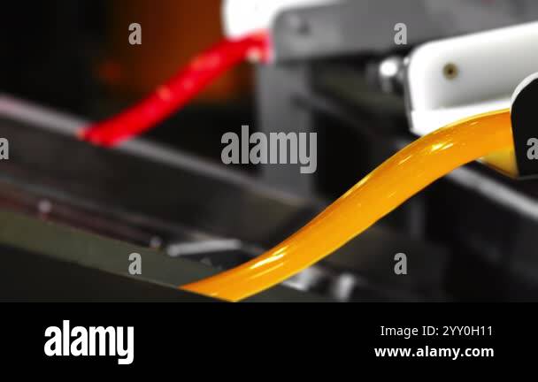 Hot orange and red liquid caramel on a conveyor belt for the production ...
