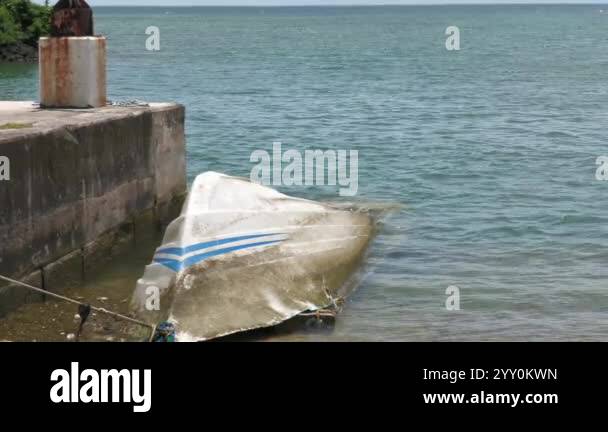 Steady footage of a pier at low tide, with an overturned boat half ...