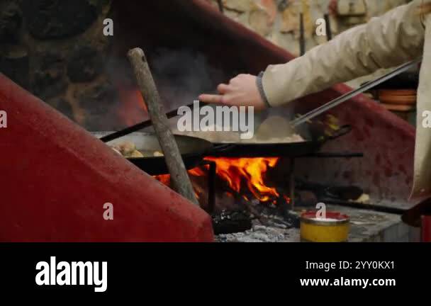 Chefs in casual clothes mix ingredients cooking Paella. Open fire heats ...