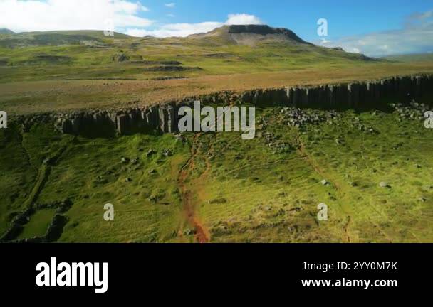 High cliff cuts across expand green grassy field on sunny day in summer ...