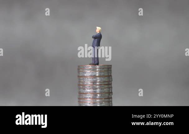 Miniature entrepreneur on piles of coins. A miniature man standing on a ...