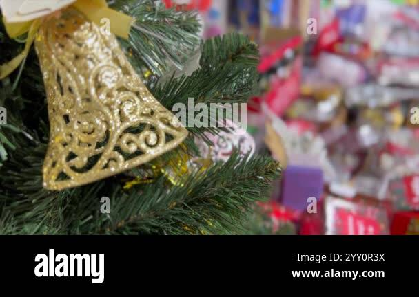 Golden bell hanging on a Christmas tree branch with blurred gift boxes ...
