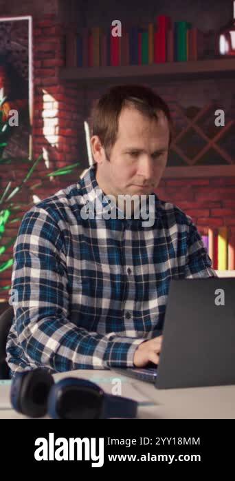 Man seated at home office desk using laptop, checking emails displayed ...