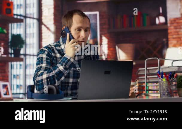 Manager in home office sitting at desk in front of laptop, calling ...