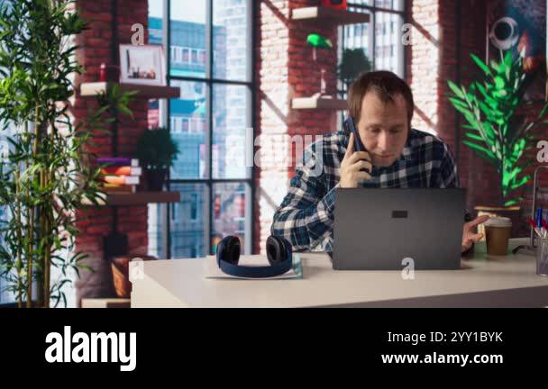 Manager in home office sitting at desk in front of laptop, calling ...