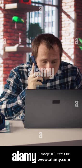 Manager in home office sitting at desk in front of laptop, calling ...