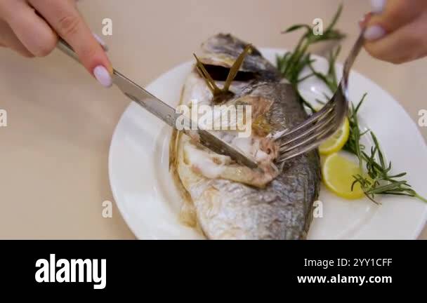 On a plate there is baked sea fish with vegetables and herbs prepared ...