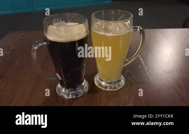 Beer is pouring into a two beer mugs with bubbles close-up on a black ...