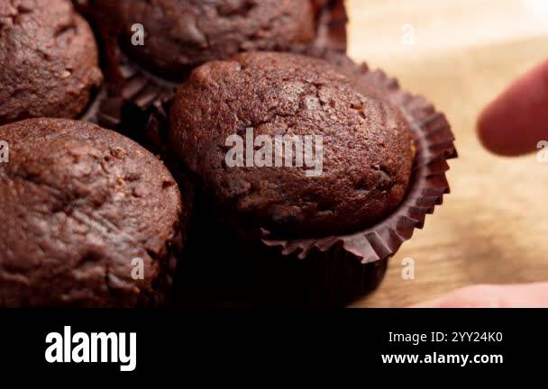Hand picking up a freshly baked chocolate cupcake with cocoa texture in ...