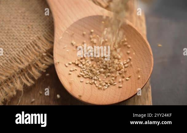 Close up of organic sesame seeds falling into a wooden spoon placed on ...