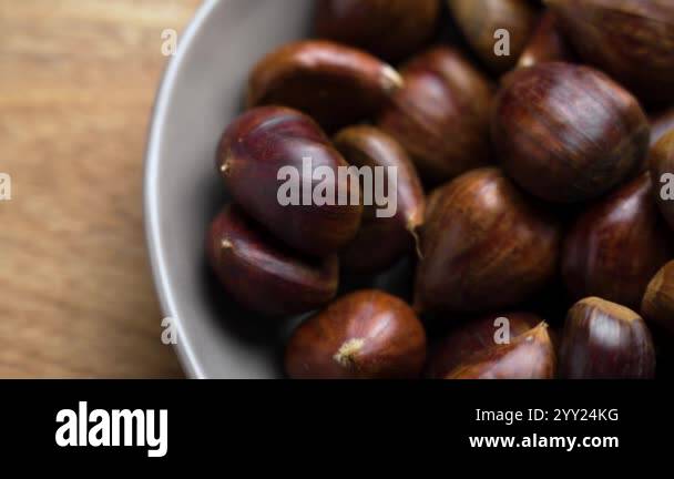 Whole unpeeled raw chestnut fruits with dark brown shells falling into ...
