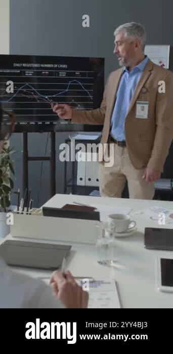 Vertical shot of middle-aged man pointing at chart on screen and ...