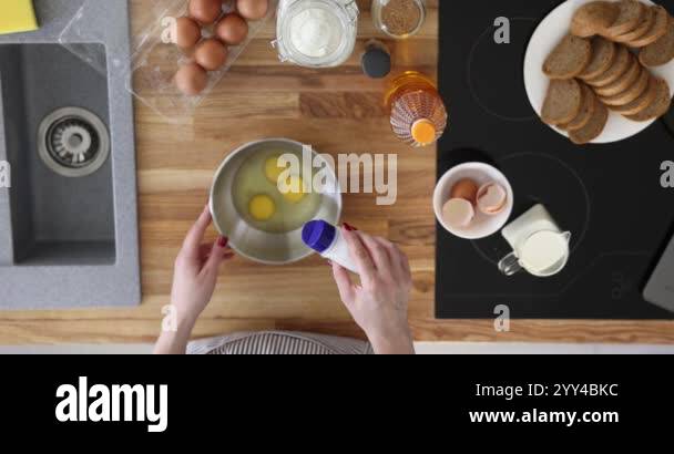 Cook woman adding salt to eggs in bowl in kitchen top view. Delicious ...