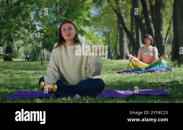 In the park two ladies exercise abs workout on the grass using the yoga mat they take the ...