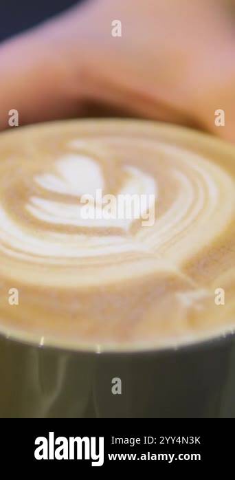 Womans hands take cup of coffee and raise it above the table, rosetta ...