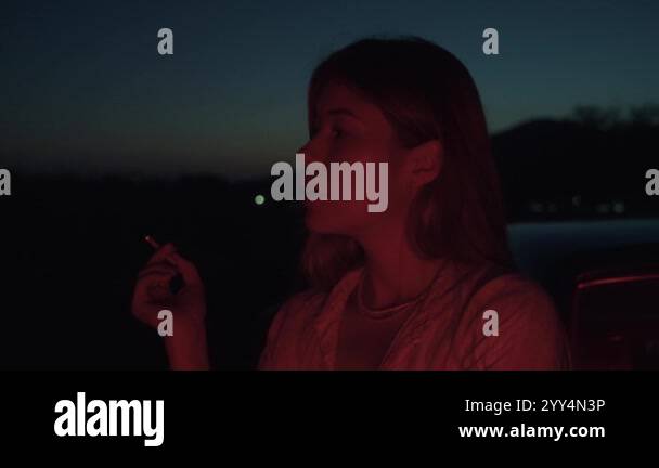 A woman enjoys a quiet moment while smoking in twilight, capturing an ...