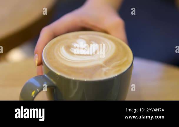 Womans hands take cup of coffee and raise it above the table, rosetta ...