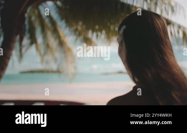 A woman standing upright on a sandy beach close to a tall palm tree ...