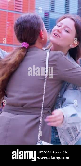 young women share a heartfelt hug in a vibrant urban environment. Their ...