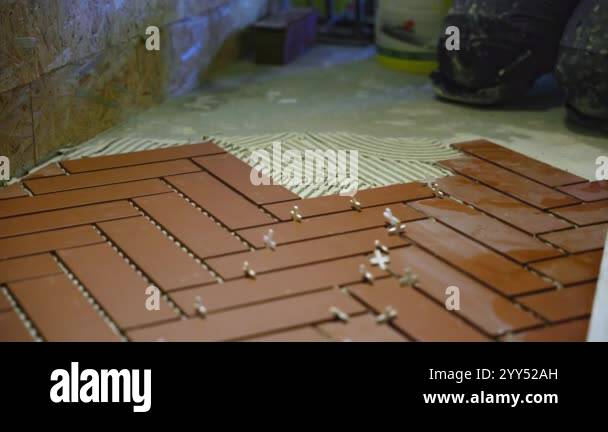 Hands place red brick tiles in a herringbone pattern indoors, using ...