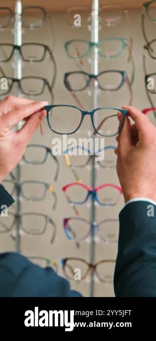 A man in a suit carefully examines a pair of eyeglasses, holding them ...