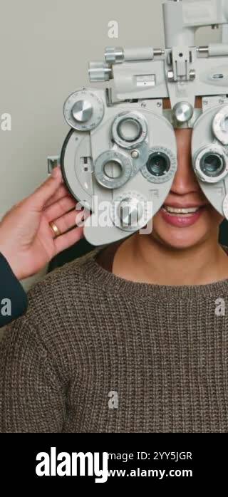 A young woman getting her eyes checked by an optometrist. She looks through a phoropter during ...