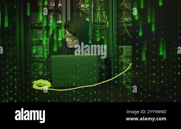 Hooded person using laptop over green binary code animation in server ...