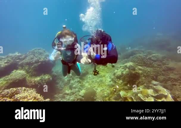 Two scuba divers, a child and an adult man, swim underwater showing the ...