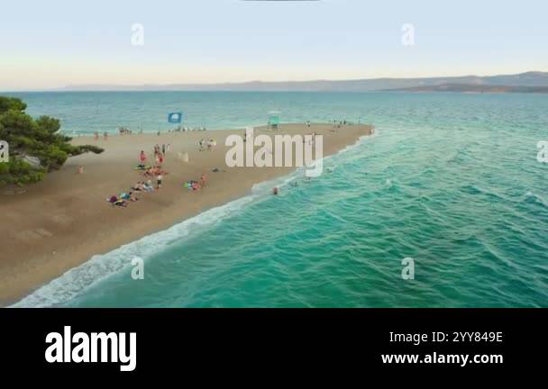 Zlatni Rat beach at sunset. People swim in the sea, swinging on the ...