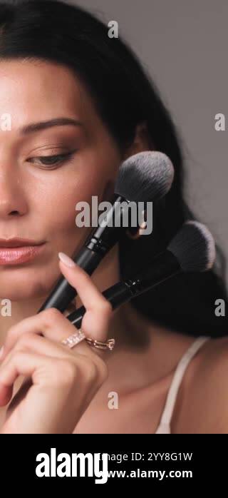Portrait of a brunette woman with glowing, flawless skin holding makeup ...