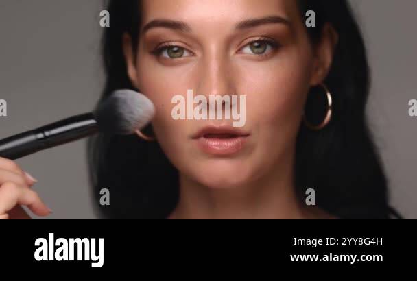 Close-up of a sophisticated woman applying makeup with a brush ...