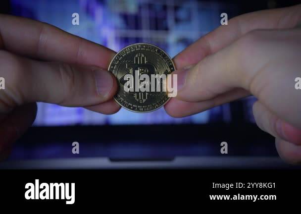 A person is holding a shiny gold coin that symbolizes cryptocurrency in ...