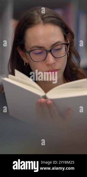 A young woman is reading intently in a library, showcasing her deep ...