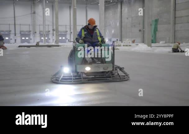 A skilled worker operates a concrete finishing machine to smooth a ...