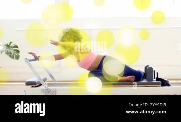 Exercising on Pilates reformer, woman surrounded by yellow bubbles ...