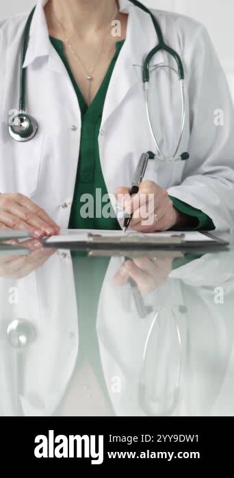 Woman doctor using a clipboard and taking notes on glass desk in a ...