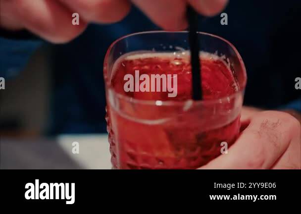 Close up of a man mixing a red cocktail with a black straw Stock Video ...