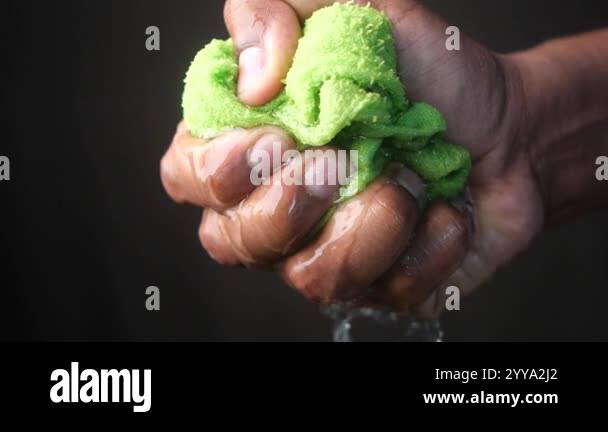 Hands squeeze wet towel against black background. draining water from ...
