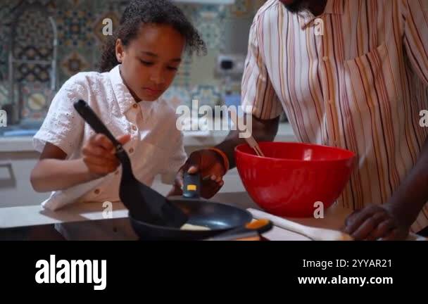 African American father man hand frying pancakes together with daughter ...
