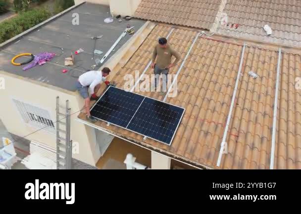 Drone view of workers positioning solar panels on a red-tiled roof in ...