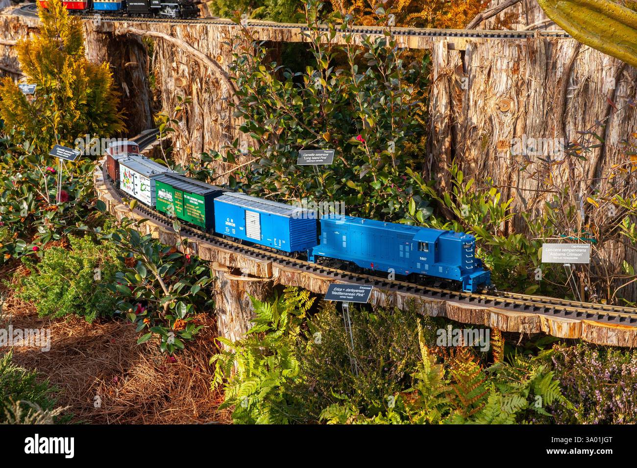 A model freight train winds through lush greenery on a railway bridge ...