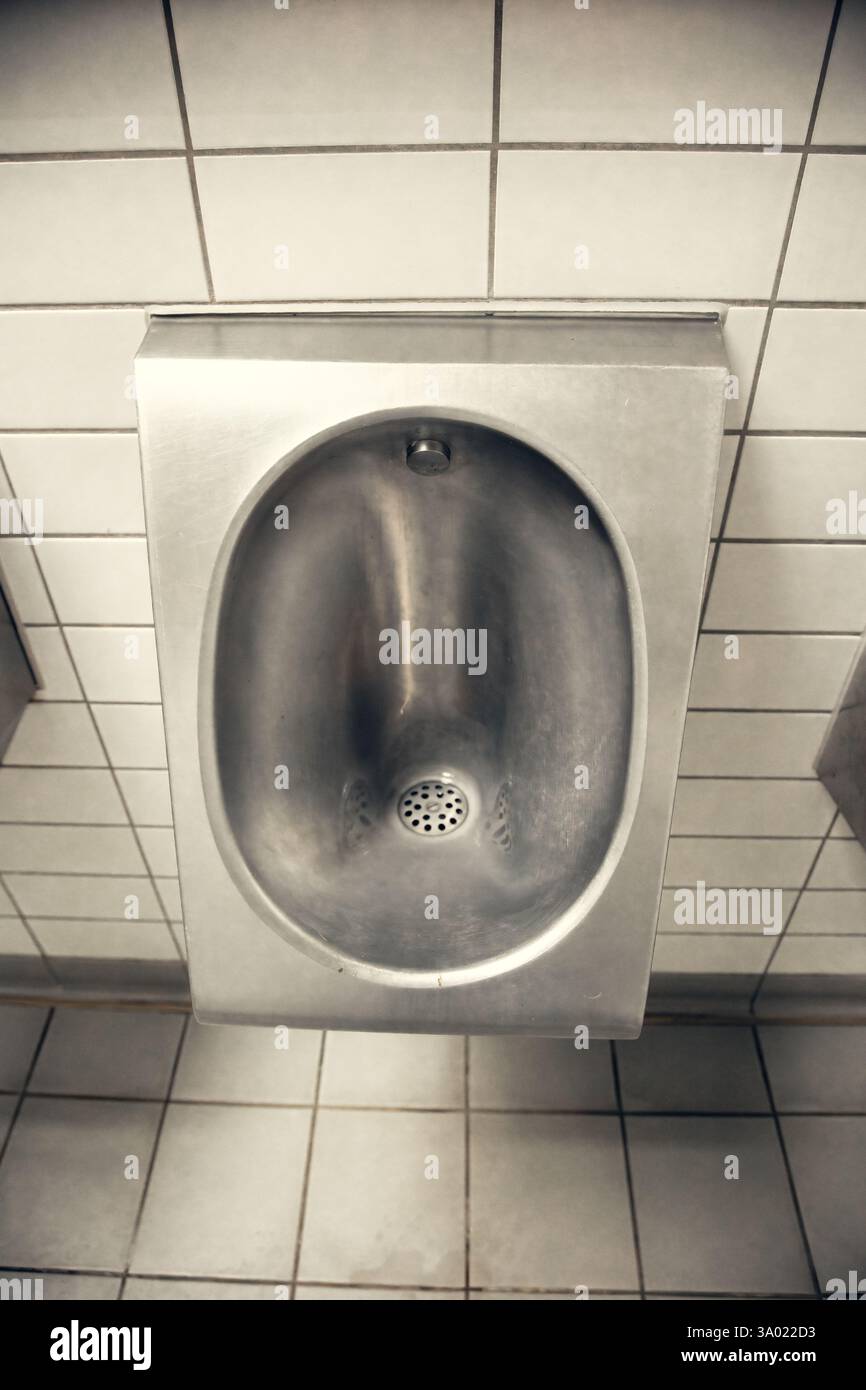 A stainless steel urinal installed in a public restroom with white ...