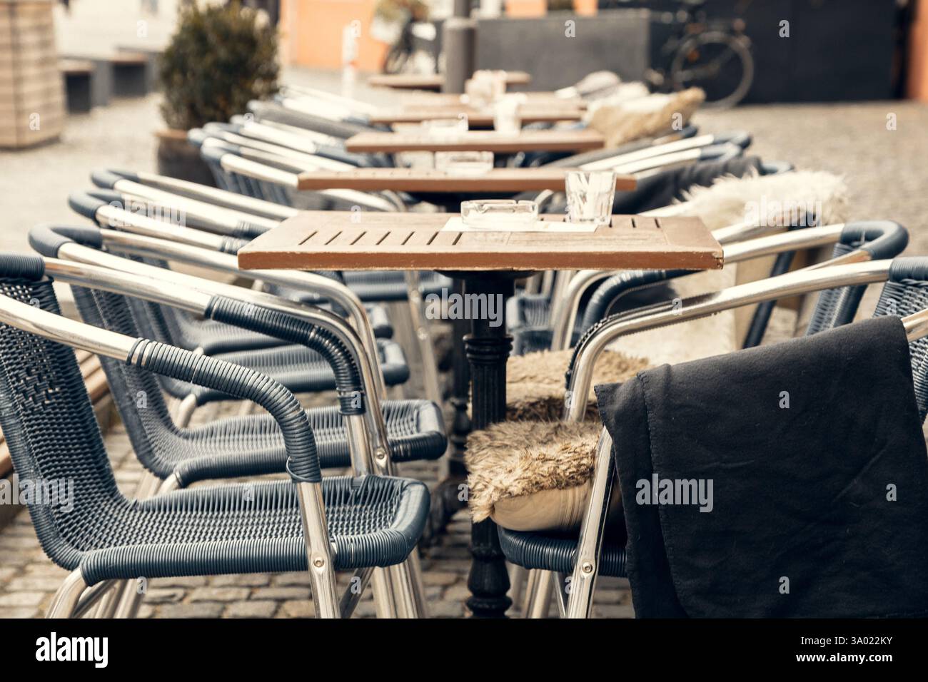 A charming outdoor cafe with empty tables and woven chairs on a cobblestone street in a European ...