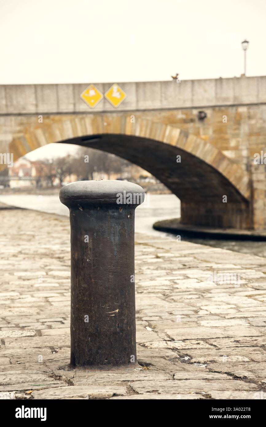 A weathered mooring bollard on an old cobblestone riverbank with a ...