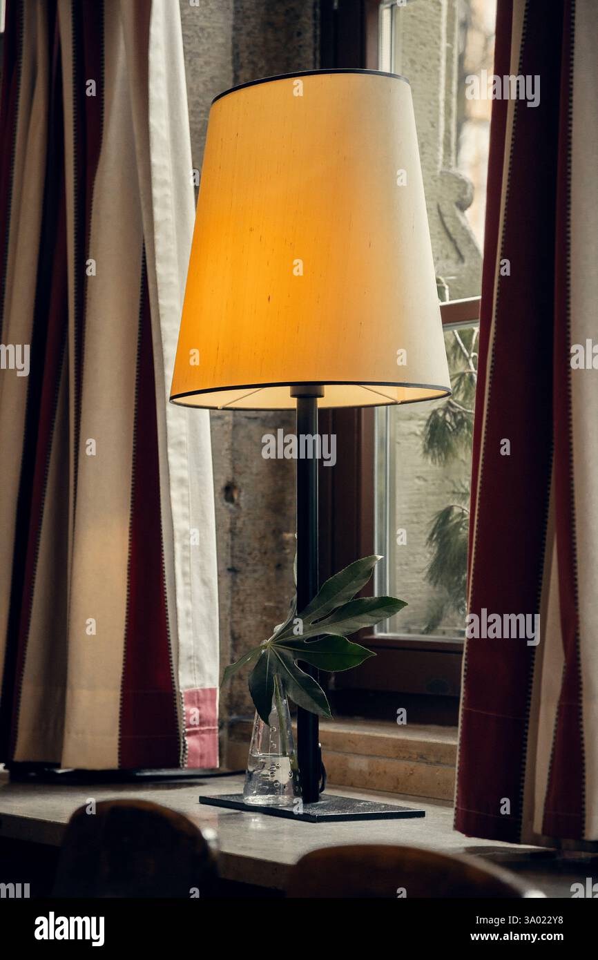 A warmly lit table lamp standing by a window in a rustic interior with ...