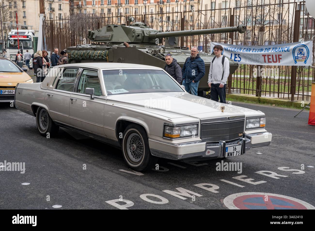 Vintage car driving past a military tank on a busy urban street in ...